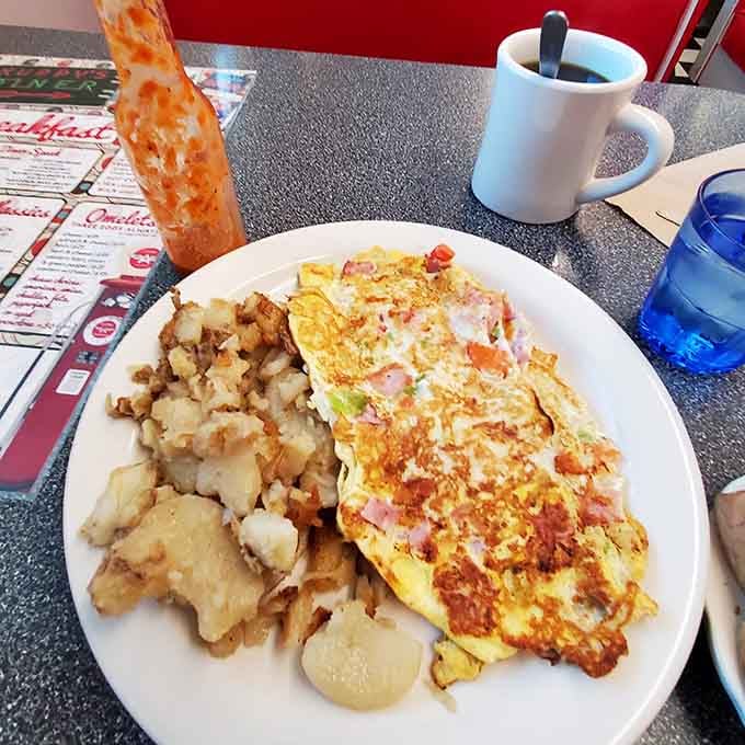 A western omelet packed with ham, peppers, and onion, sitting next to a mountain of golden home fries.