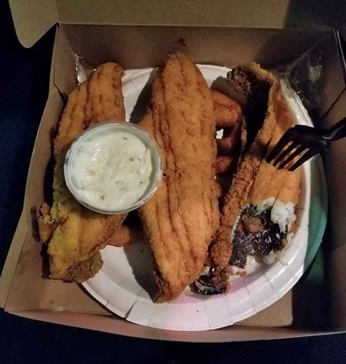 Catfish and a bite taken from it sharing a takeout box like old friends. Comfort food at its most unapologetic best.