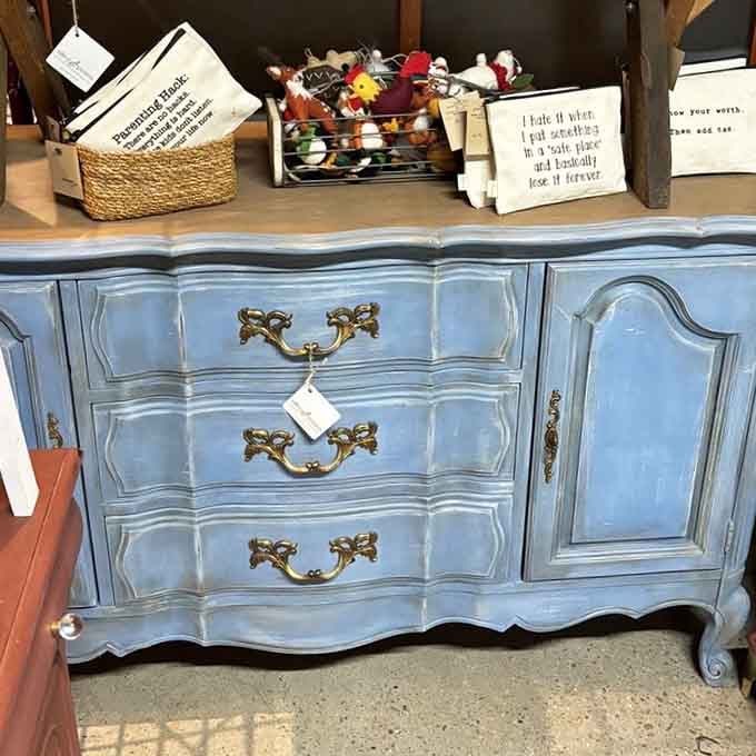 That dusty blue French provincial dresser with brass hardware is basically furniture's answer to a classic movie star.