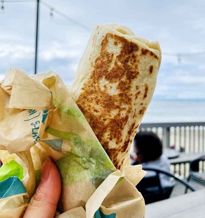 A Burrito Supreme held up against a backdrop of actual Pacific Ocean waves. This is not a drill.