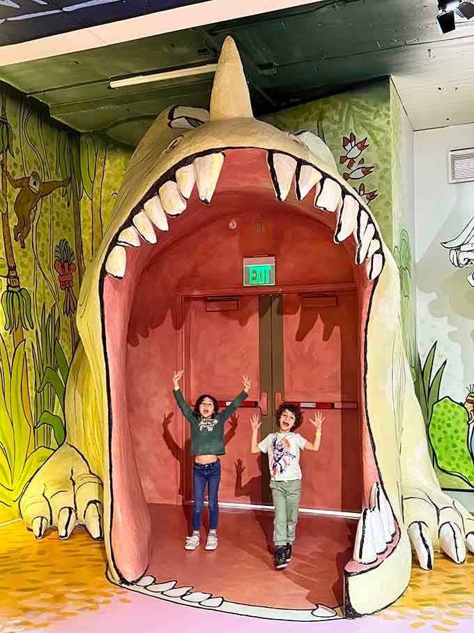 Two kids standing inside a giant monster's mouth, arms raised in triumph — parenting goals, honestly.