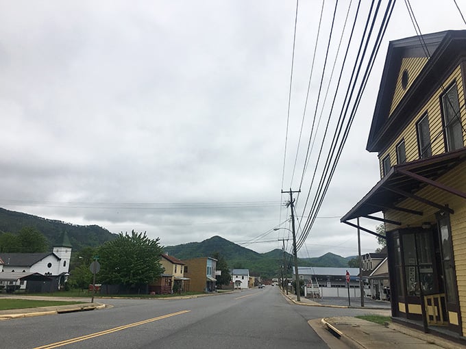 A quiet street curves past quaint local buildings, leading your eyes toward the beautiful, mist-covered mountains in the distance.