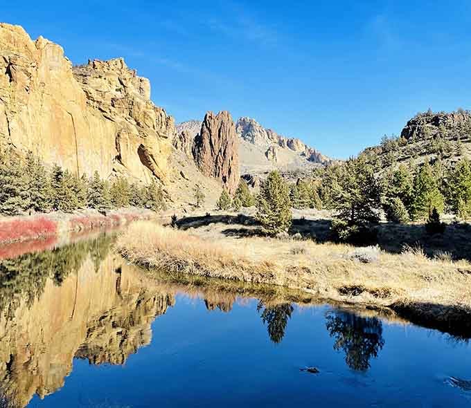 Morning light catches the towering cliffs while the Crooked River mirrors every detail in its glassy surface.