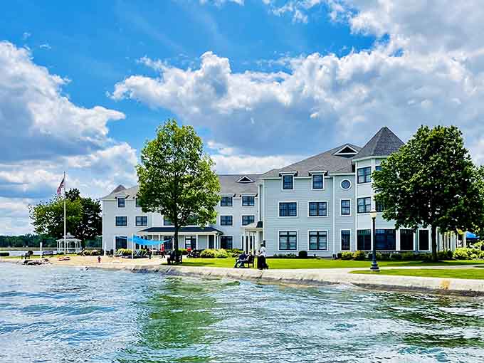 Guests relax on the grassy shoreline under fluffy white clouds, enjoying a perfect summer afternoon by the water.