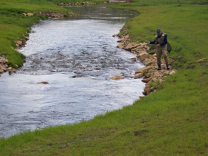 A lone angler works the rocky riverbank, finding the kind of peaceful focus that no app can replicate.