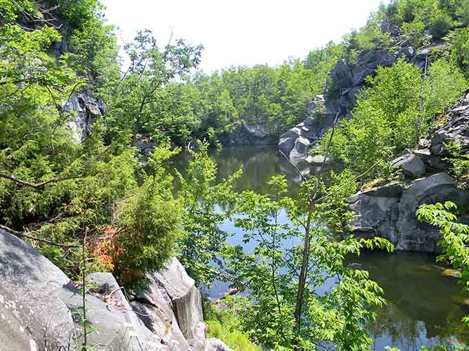That flooded quarry pit, cradled by sheer granite walls and lush green trees, looks almost too beautiful to be real.