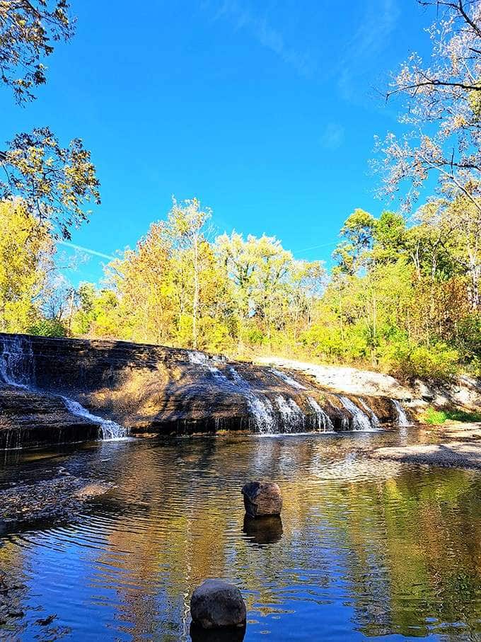 Autumn gold reflects perfectly in the still pool below, turning this quiet waterfall into a mirror of the season.