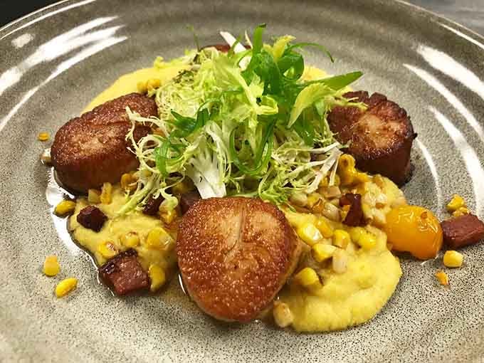 Pan-seared scallops rest on vibrant accompaniments, plated with the kind of care that makes you pause before diving in.