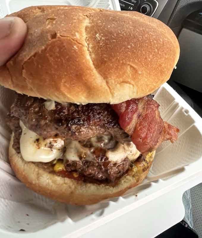 This double bacon cheeseburger towers like edible architecture, defying both gravity and your willpower to share it.