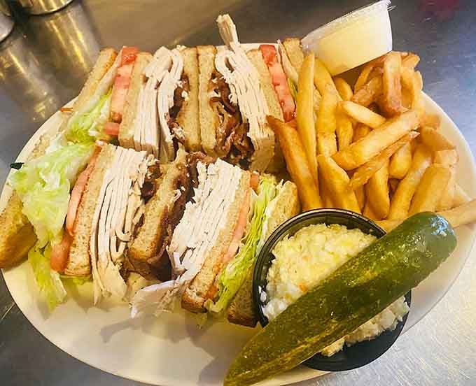 A proper club sandwich with fries, a pickle, and coleslaw, the holy trinity of diner lunch.
