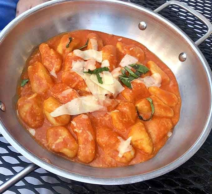 Pillowy gnocchi nestled in a vibrant tomato sauce, served straight from the pan with fresh basil and shaved parmigiano. Comfort food with real credentials.