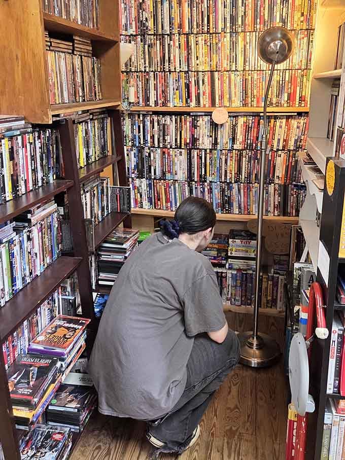 Someone crouching in a corner surrounded by DVDs is either a serious collector or having the best day.