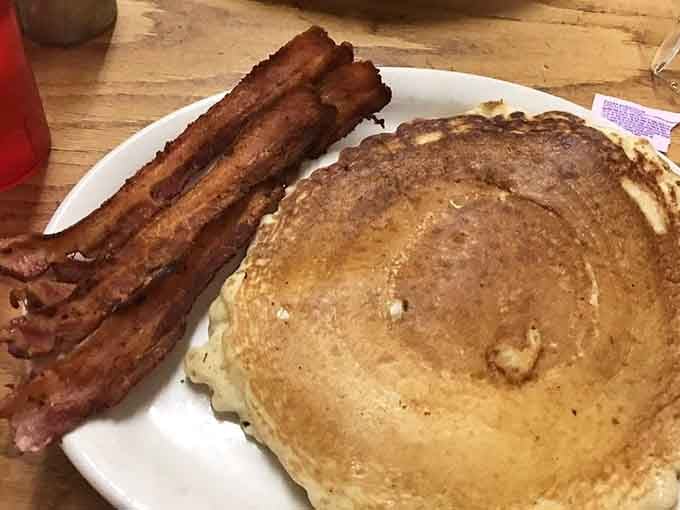 A golden pancake the size of a hubcap beside three strips of crackling bacon, breakfast doesn't get more honest than this.