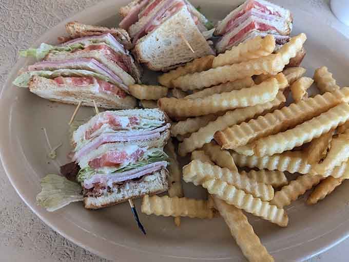 A proper club sandwich stacked tall and honest, served with crinkle-cut fries that mean serious business.