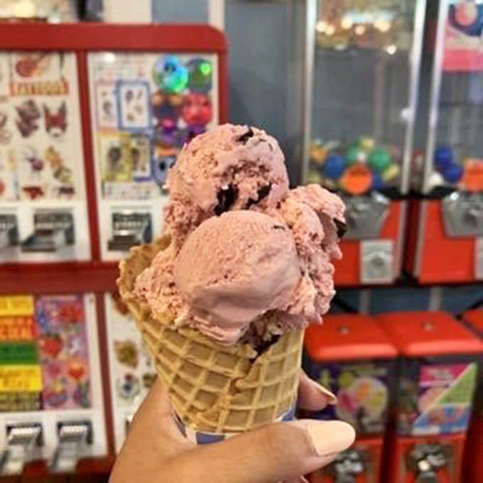 Three scoops of Raspberry Chocolate Chip on a waffle cone, with gumball machines cheering from behind. Perfect setting.