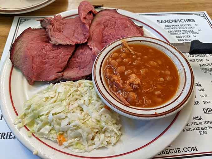 Sliced barbecue beef alongside a bowl of BBQ beans and a heap of cole slaw. Southern comfort, served without ceremony.