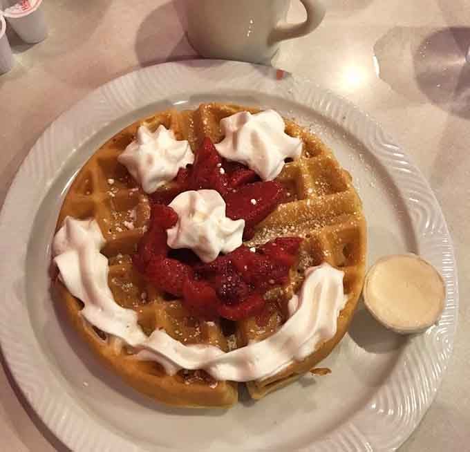 A golden waffle topped with strawberries and whipped cream, dessert for breakfast, and absolutely nobody is complaining.