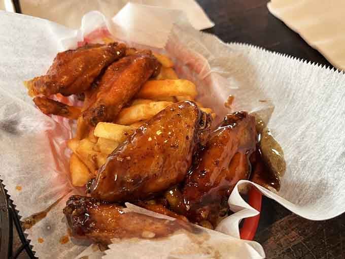 Glossy, saucy wings piled over golden fries in a basket. These wings arrived looking like pure, unapologetic joy.