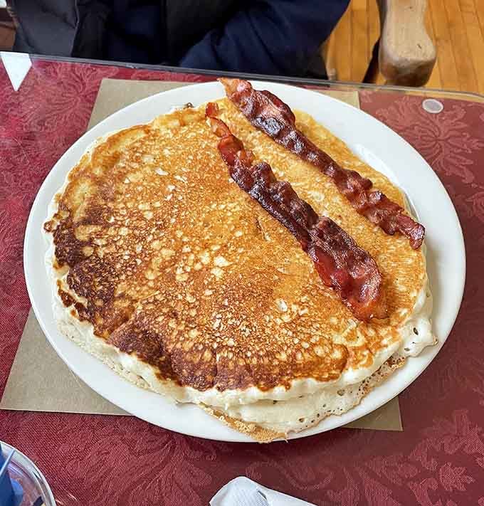 A pancake the size of a hubcap with two strips of perfectly crisped bacon. Breakfast doesn't negotiate, it delivers.