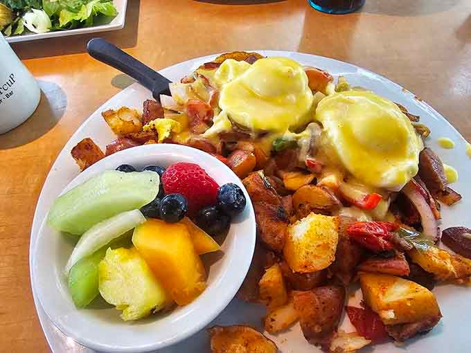 Silky hollandaise draped over eggs Benedict, surrounded by crispy potatoes and fresh fruit. This plate means serious business.