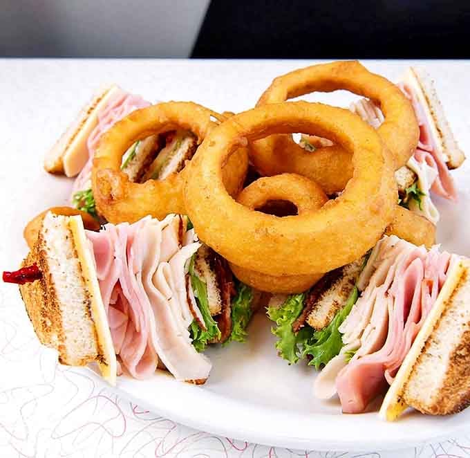 A club sandwich stacked generously high, flanked by golden onion rings. Lunch never looked this confident.