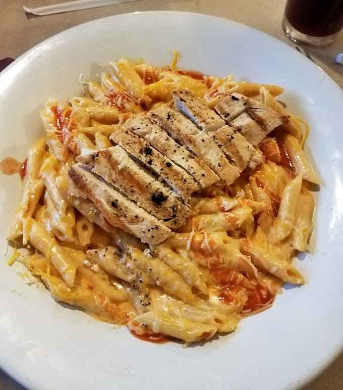 Penne pasta topped with grilled chicken in a rich, saucy bowl that looks like a warm hug you can eat.