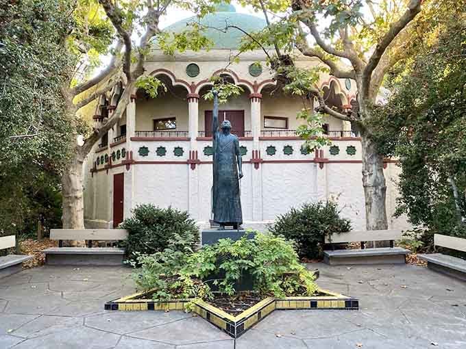 A bronze statue stands serenely in the garden, surrounded by trees, proof that great thinkers deserve great monuments in peaceful settings.