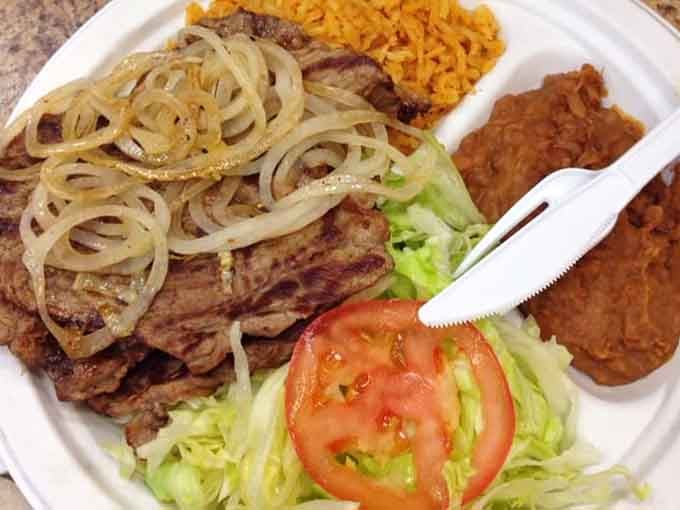 Grilled carne asada with caramelized onions, rice, and beans creates the kind of plate that haunts your dreams.