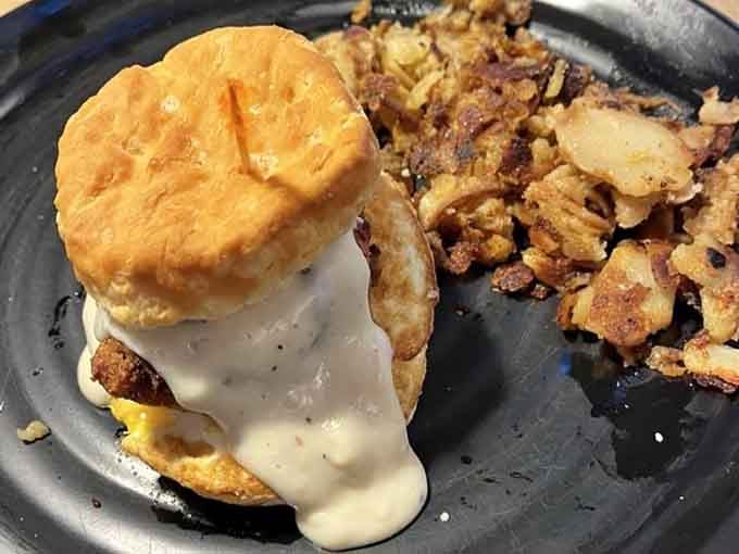Creamy gravy draped over a golden biscuit sandwich, with crispy home fries standing proudly alongside. Pure morning comfort.