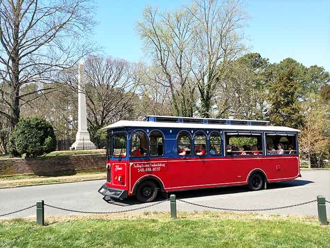 Rolling past a solemn stone monument under a crisp blue sky, this trolley reminds you that some roads carry more than just passengers.