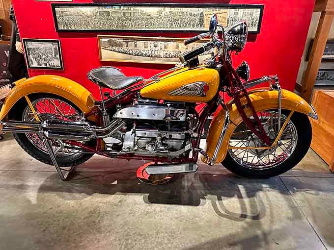 That bold yellow and chrome Indian Four-Cylinder gleams against the red wall like a sunflower that somehow learned to roar.