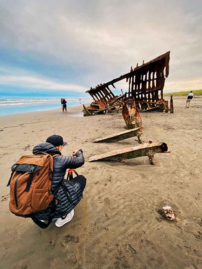 A photographer crouches beside the rusted anchor, because some subjects simply demand you get down to their level.