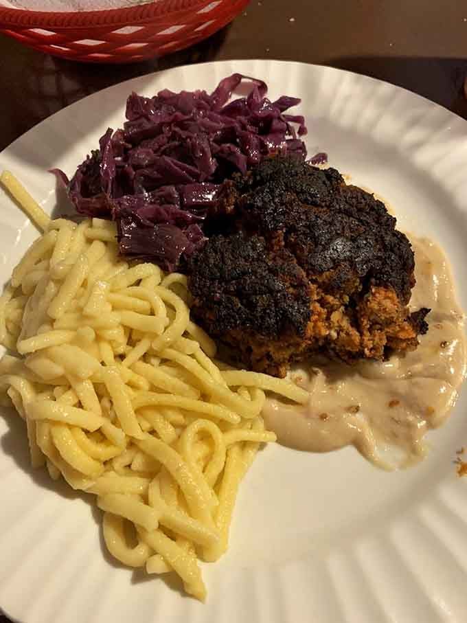 A hearty Frigadelle resting on a pool of gravy beside sp&auml;tzle and red cabbage, German comfort food at its most honest.