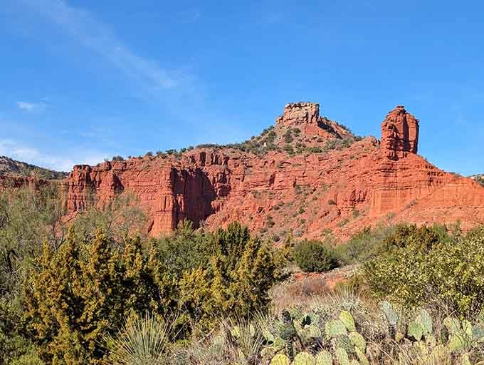 Dramatic rock formations rise from the canyon floor like ancient castles, their red walls glowing in the afternoon sunlight.