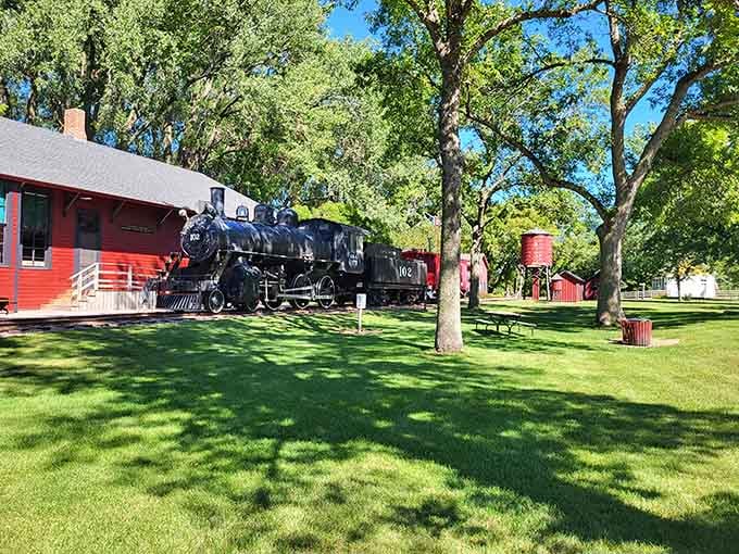 That handsome black locomotive sitting beside a cherry-red depot is basically the coolest neighbor in all of Currie.