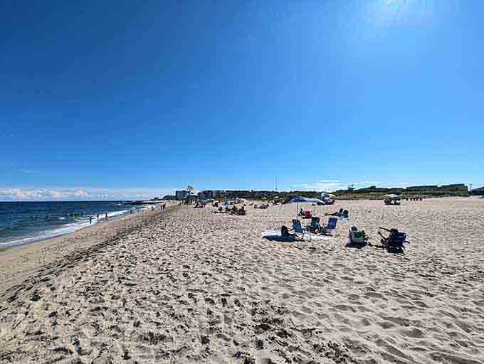 Beach chairs dot the wide sand while gentle waves roll in under endless blue summer skies.