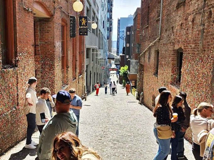 Post Alley buzzes with visitors on a sunny Seattle afternoon, all drawn to those gloriously colorful, slightly sticky brick walls.
