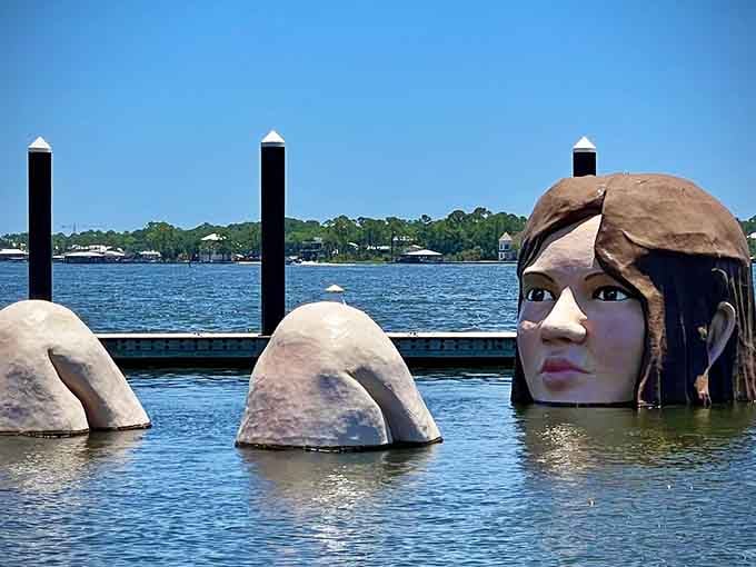 A mysterious face emerges from the water near the shore, watching boats pass with an enigmatic expression.