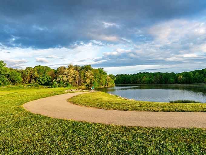 A graceful paved path sweeps around the lake's edge under a dramatic stormy sky, making Centennial Park look almost impossibly beautiful.