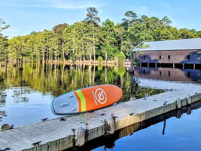 A paddleboard resting on the dock at golden hour, with the historic mill reflected perfectly in the glassy water beyond.