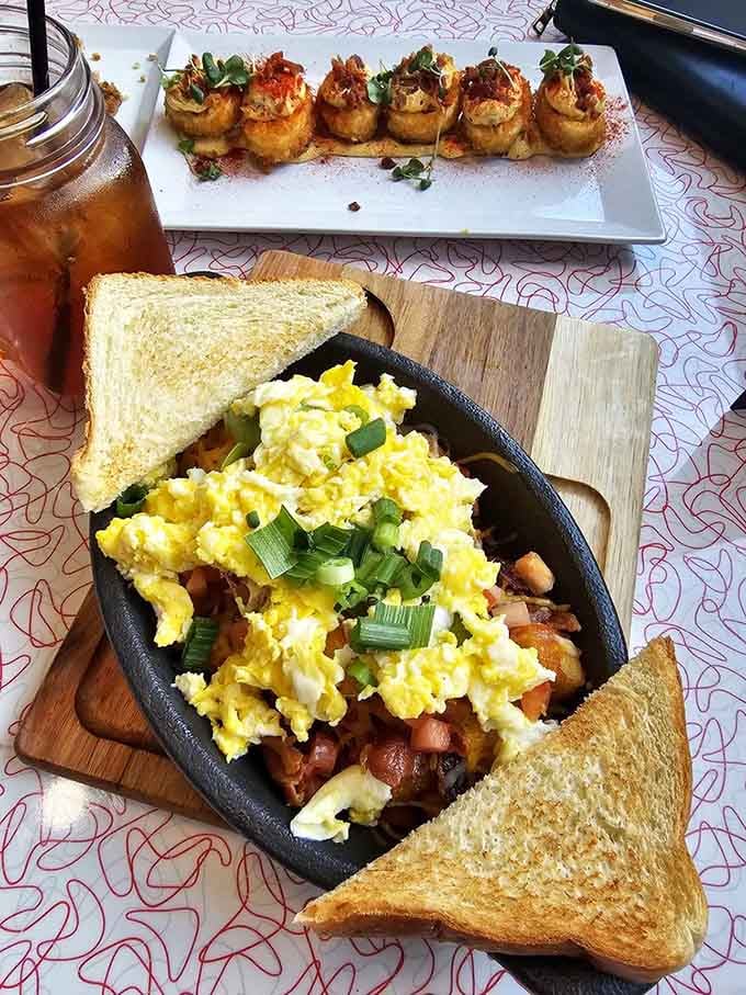 A cast iron skillet loaded with scrambled eggs, bacon, tomatoes, and green onions. Comfort food that means every word it says.