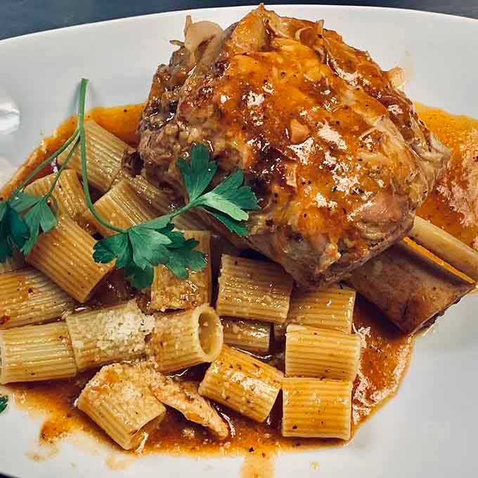 A glazed pork shank resting on mezzi rigatoni in rich braising juices, fork-tender and absolutely worth every bite.