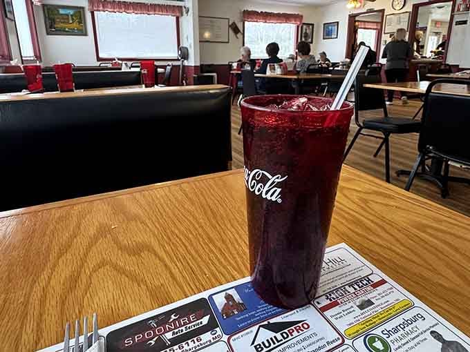 A deep red Coca-Cola glass, full of ice and something cold, sitting in a dining room that feels like a warm handshake.