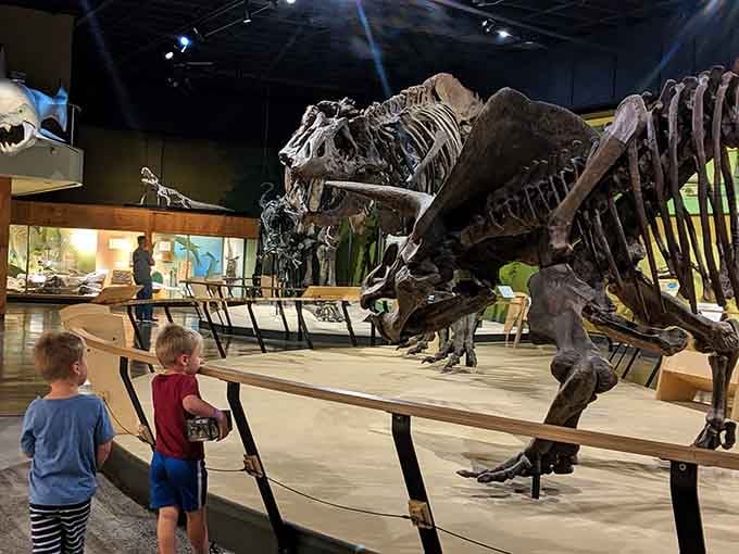 Two small visitors stand face to face with a massive dinosaur skeleton, and judging by their posture, the dinosaur is clearly winning.