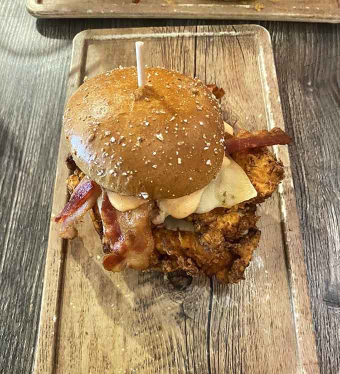 That crispy, golden fried chicken peeking out from under a seeded bun with bacon is basically a standing ovation on a cutting board.