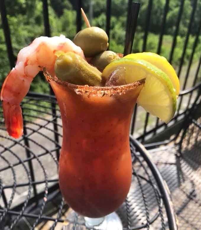 A Bloody Mary dressed for a party, complete with shrimp, olives, and a Kentucky hillside backdrop.