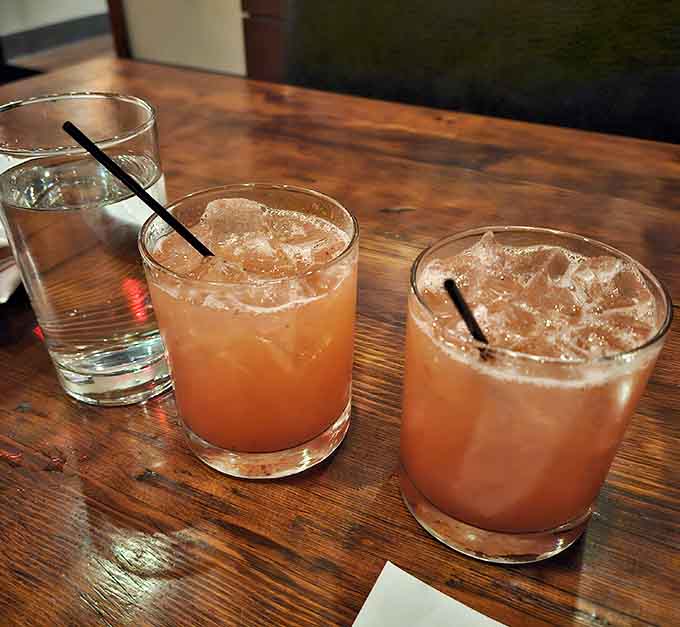 Two rosy, ice-filled cocktails on a warm wood table. This is what a good evening looks like before it even starts.