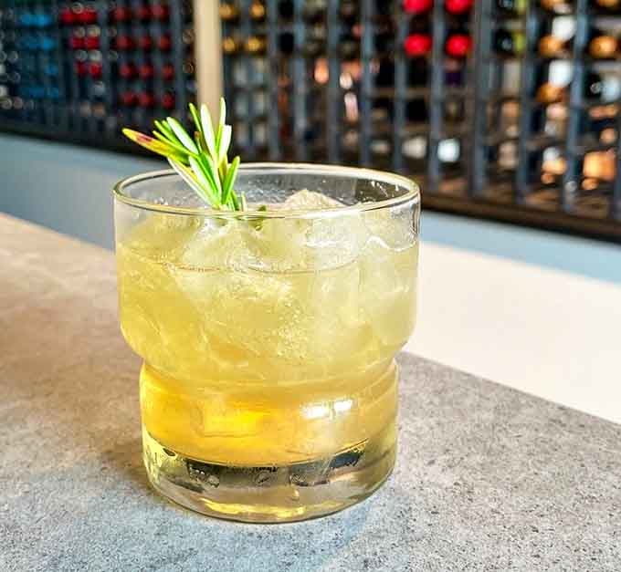 A rosemary-garnished cocktail glowing amber over crushed ice, sophisticated enough for a special occasion, relaxed enough for a Tuesday.