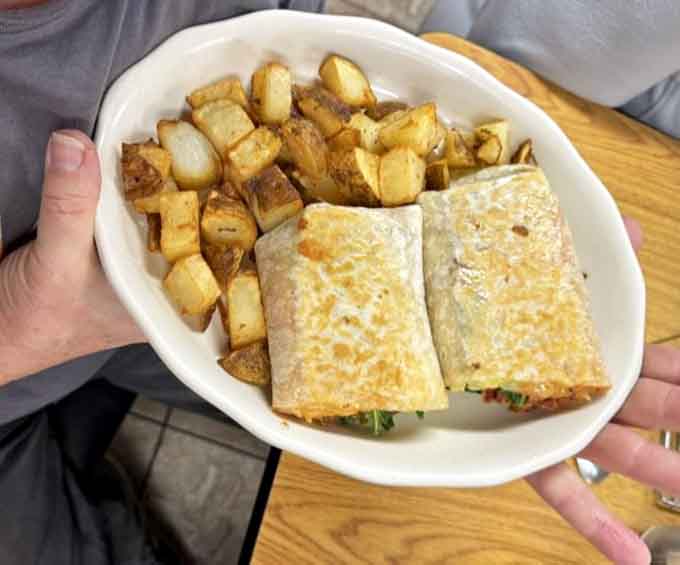 A breakfast burrito cut clean in half, stuffed full and served alongside golden homefries. Handheld happiness never looked so good.
