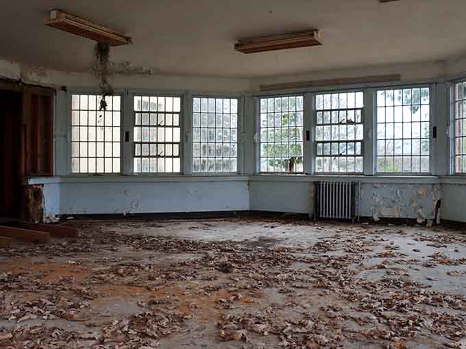 Dead leaves scattered across the floor and barred windows overhead make this room feel genuinely, deeply abandoned.
